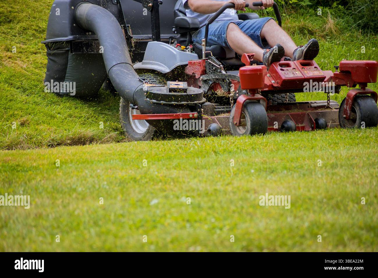 Rider operates lawn mower, cutting grass in an outdoor setting on sunny ...