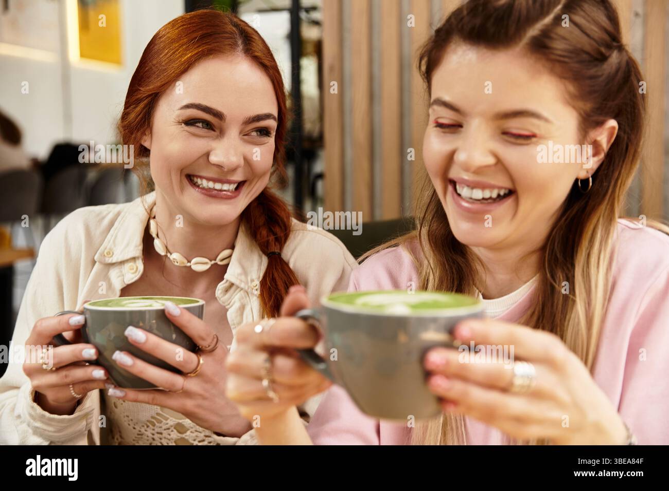Two young women laugh and enjoy delicious drinks in a stylish cafe ...