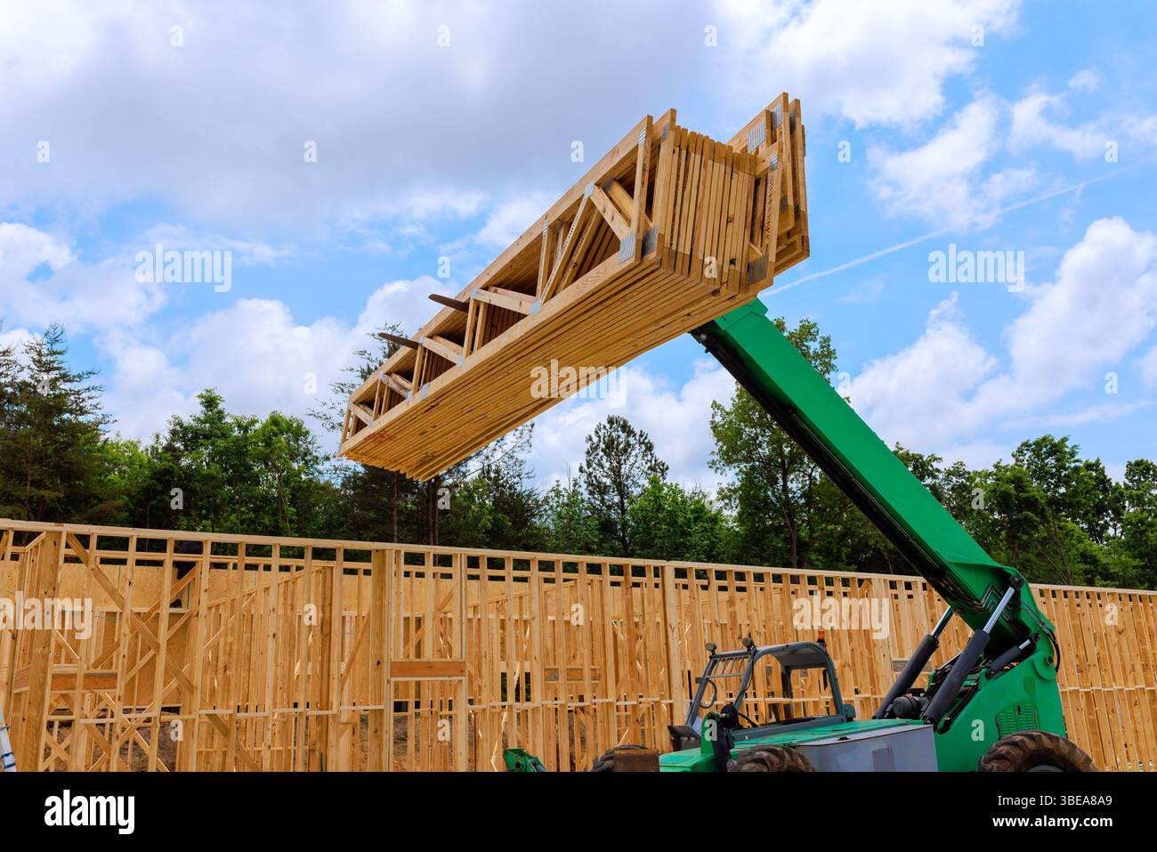 Telehandler maneuvers timber at construction area surrounded by trees ...