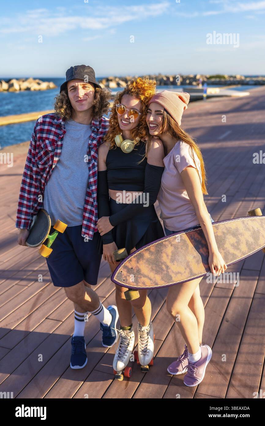 Three happy skater friends posing together on a boardwalk by the sea ...