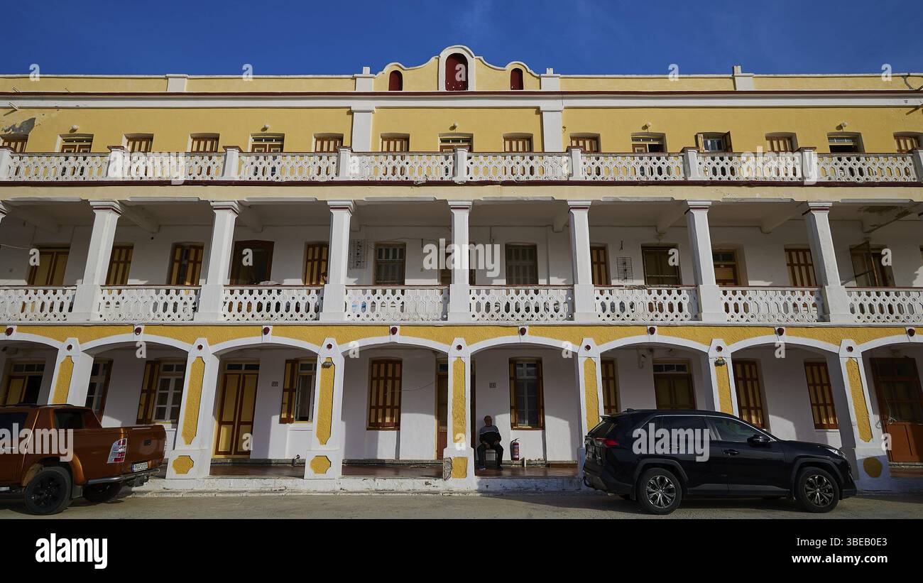 Yellow building with white balconies and parked cars in front of it ...