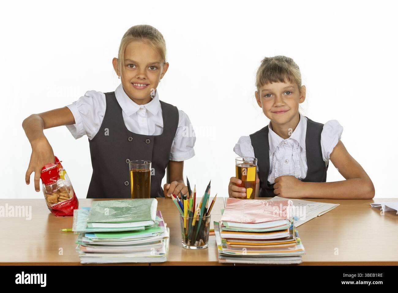 Two school girlfriends drink juice and eat cookies at a table in a ...