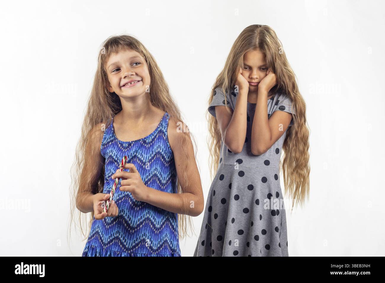 Girl joyfully holds candy, sad other girl in the background Stock Photo ...
