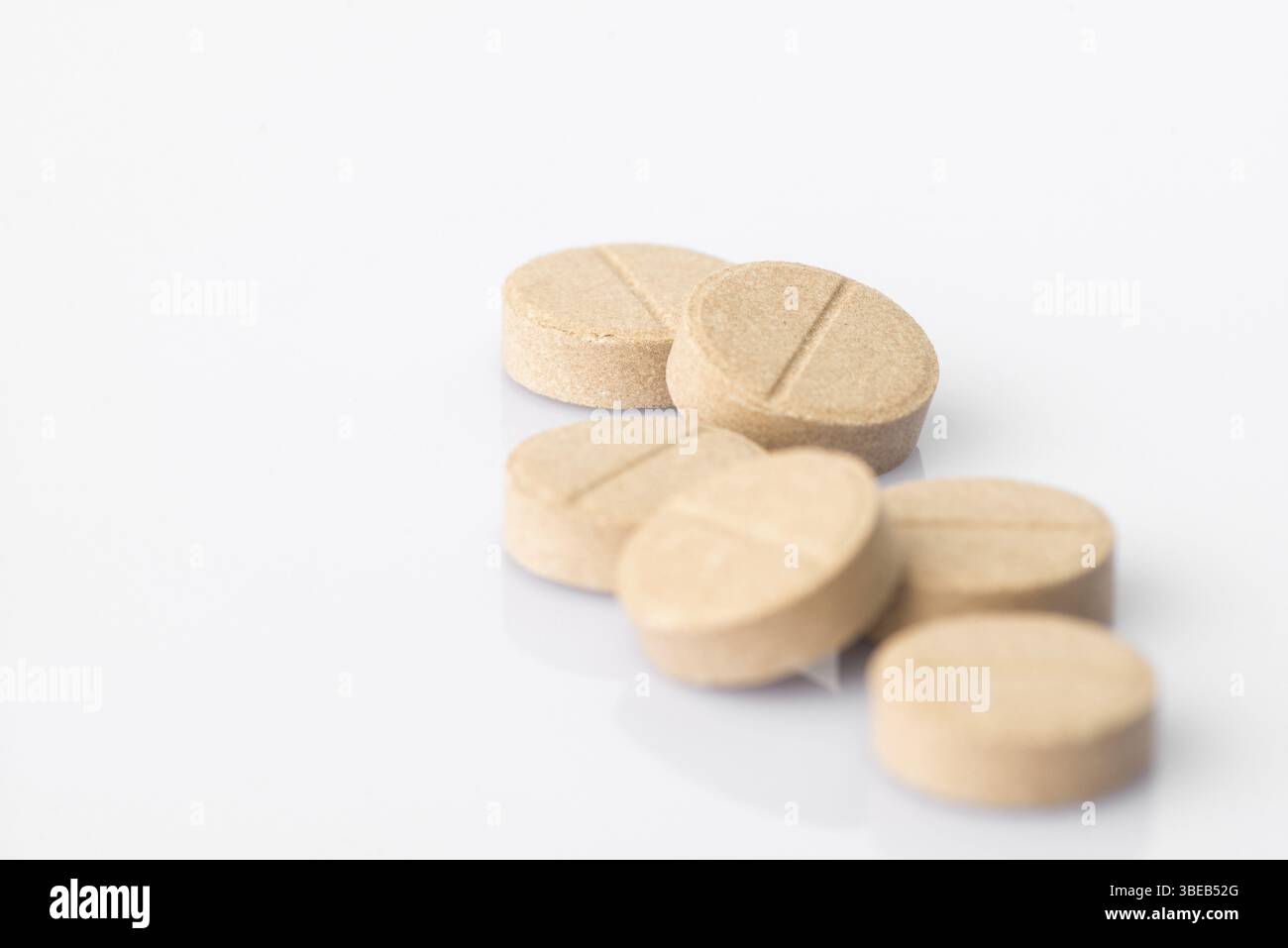 A pile of beige medical tablets on a light background. The blurred part ...