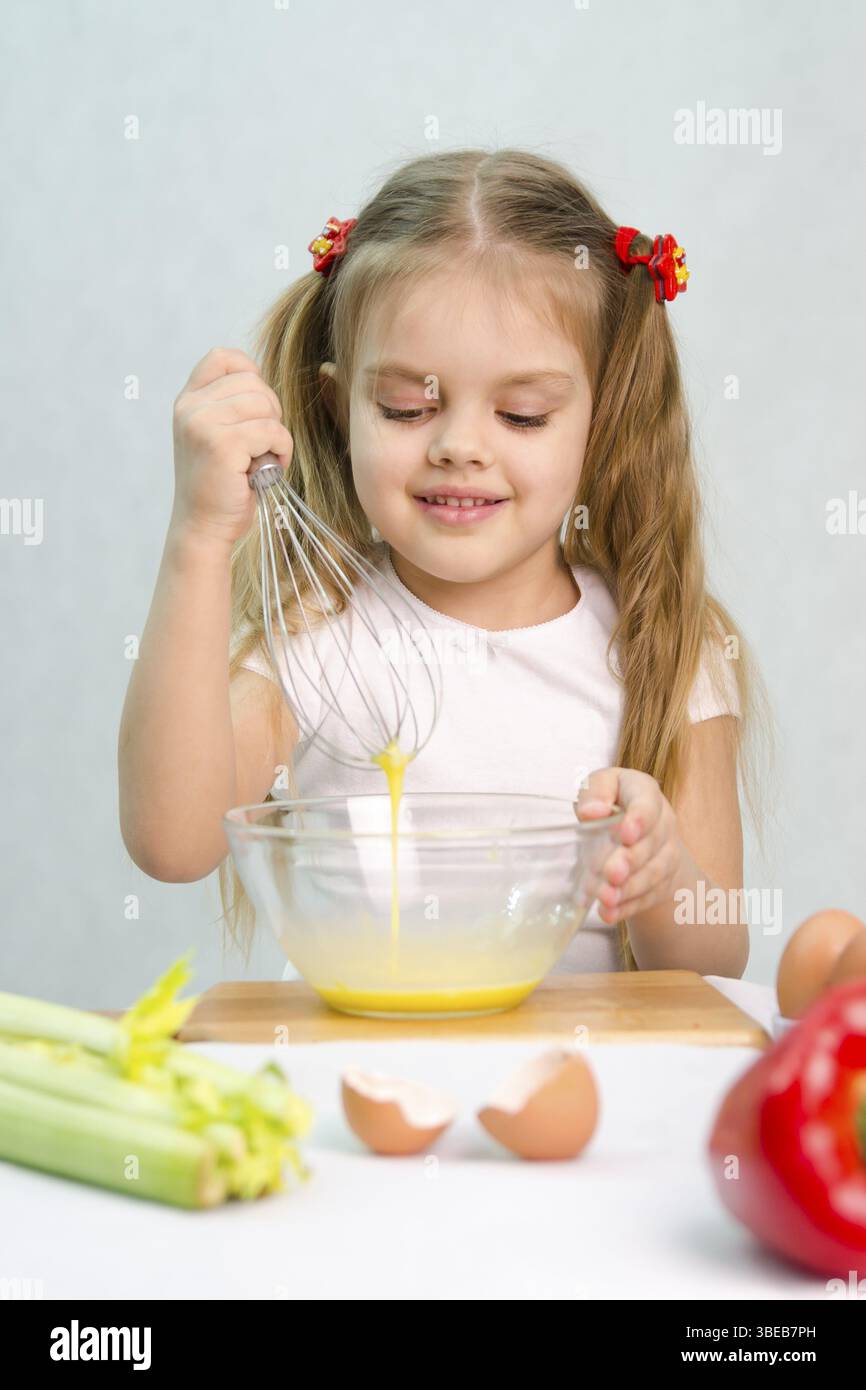 Girl playing in a cook. Girl churn whisk the eggs in a glass bowl. At ...