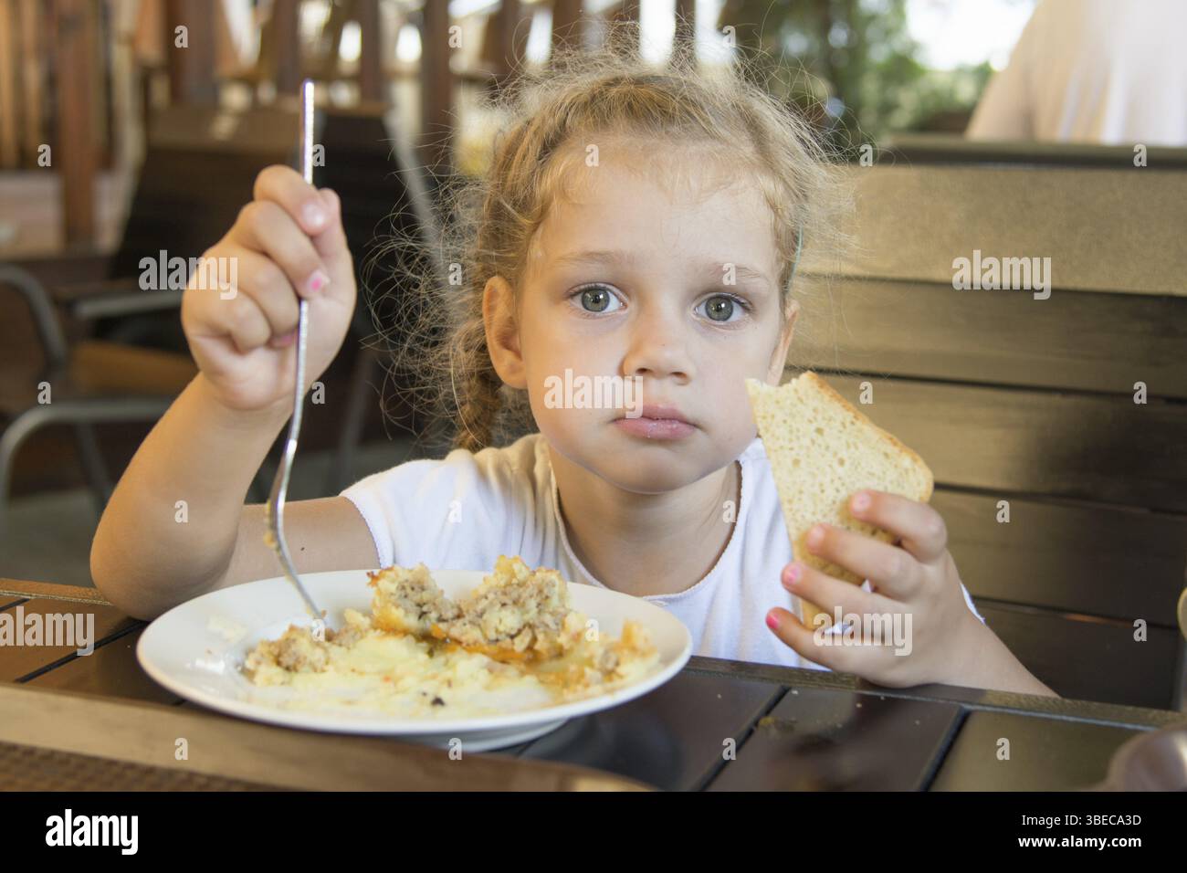 The four-year girl sits at a table and eat a main dish with bread in an ...