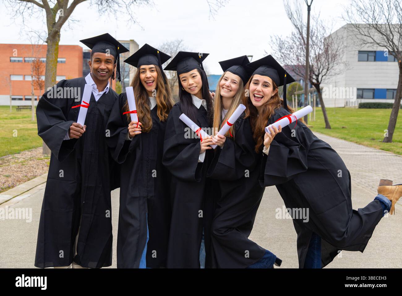 Multi ethnic graduating students wearing gowns and caps holding ...