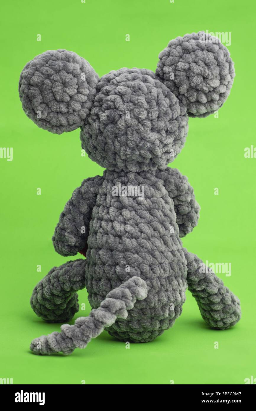 Grey knitted mouse with a heart in hand on a green background, rear ...