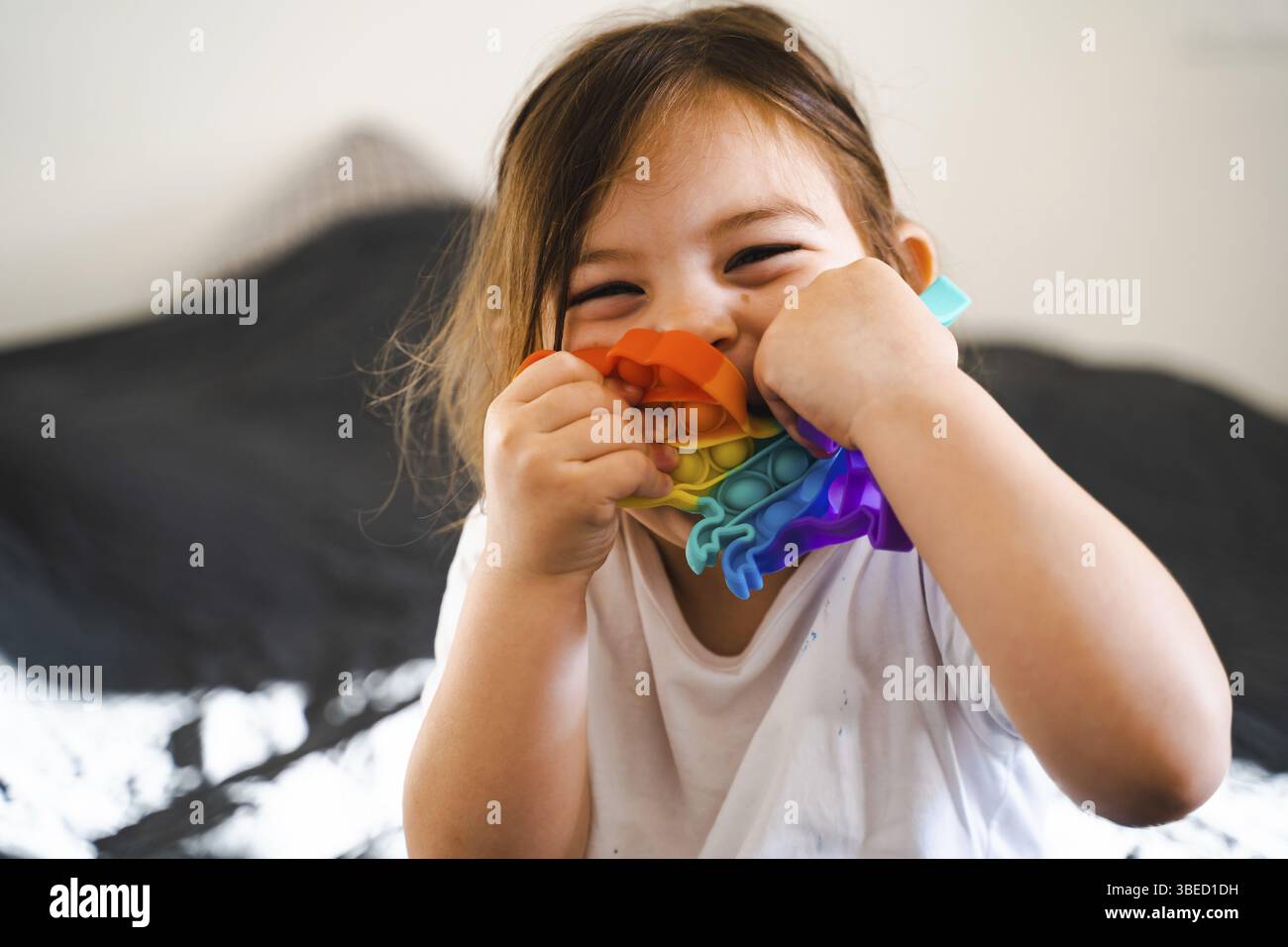 Toddler girl with popit toy in rainbow colours. Dino shape silicone toy ...