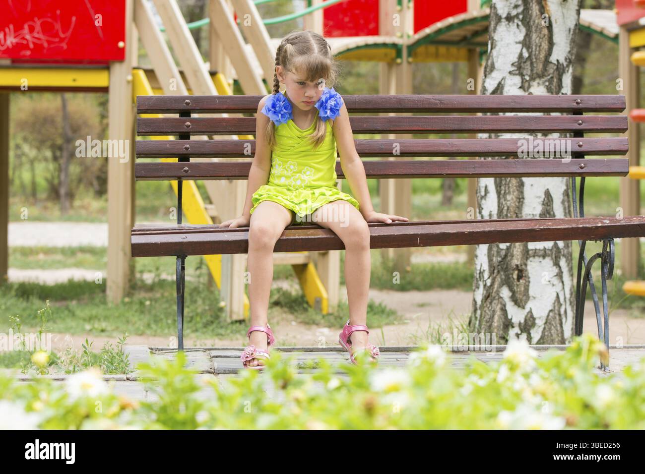 Crying girl sitting on the bench on the background of the playground ...