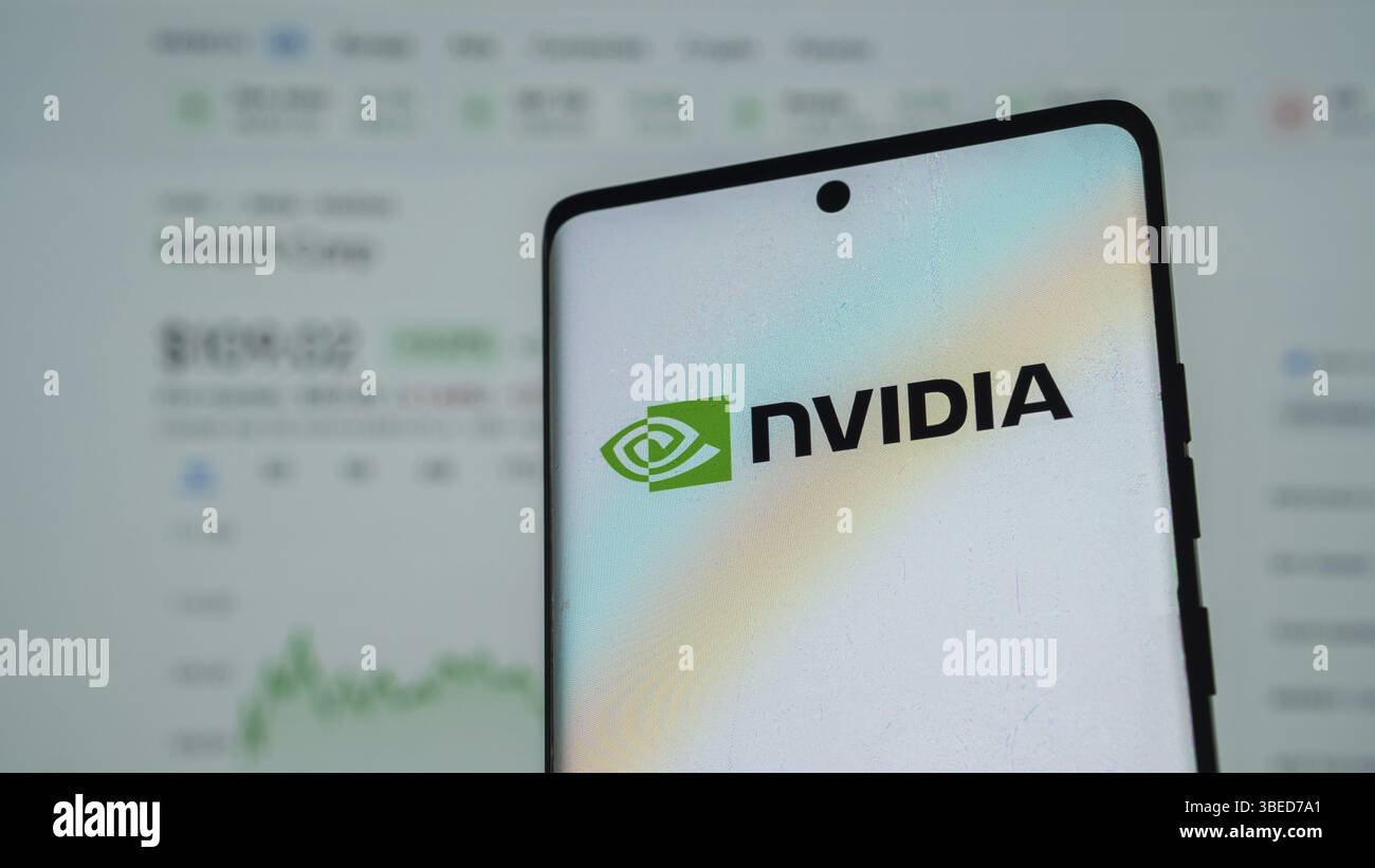 Smartphone displaying Nvidia logo with a blurred financial stock graph ...