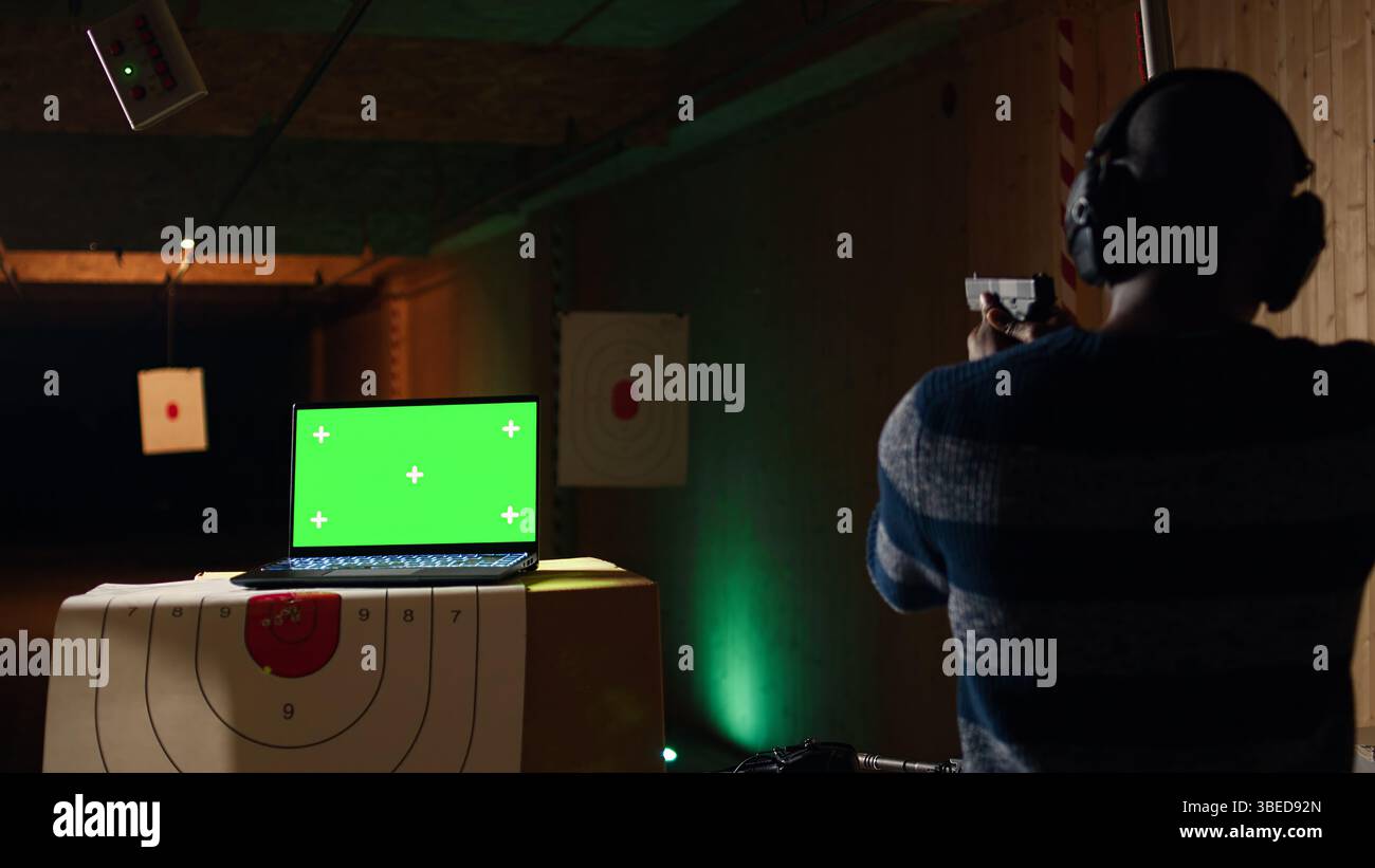 Green screen laptop next to man in firing range pressing mechanism to ...