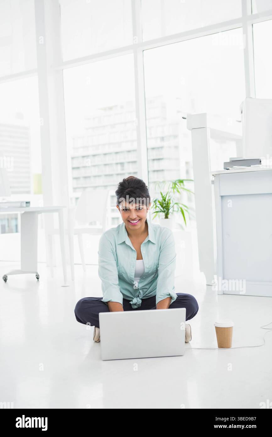 Indian woman sitting cross-legged on office floor typing on laptop with ...