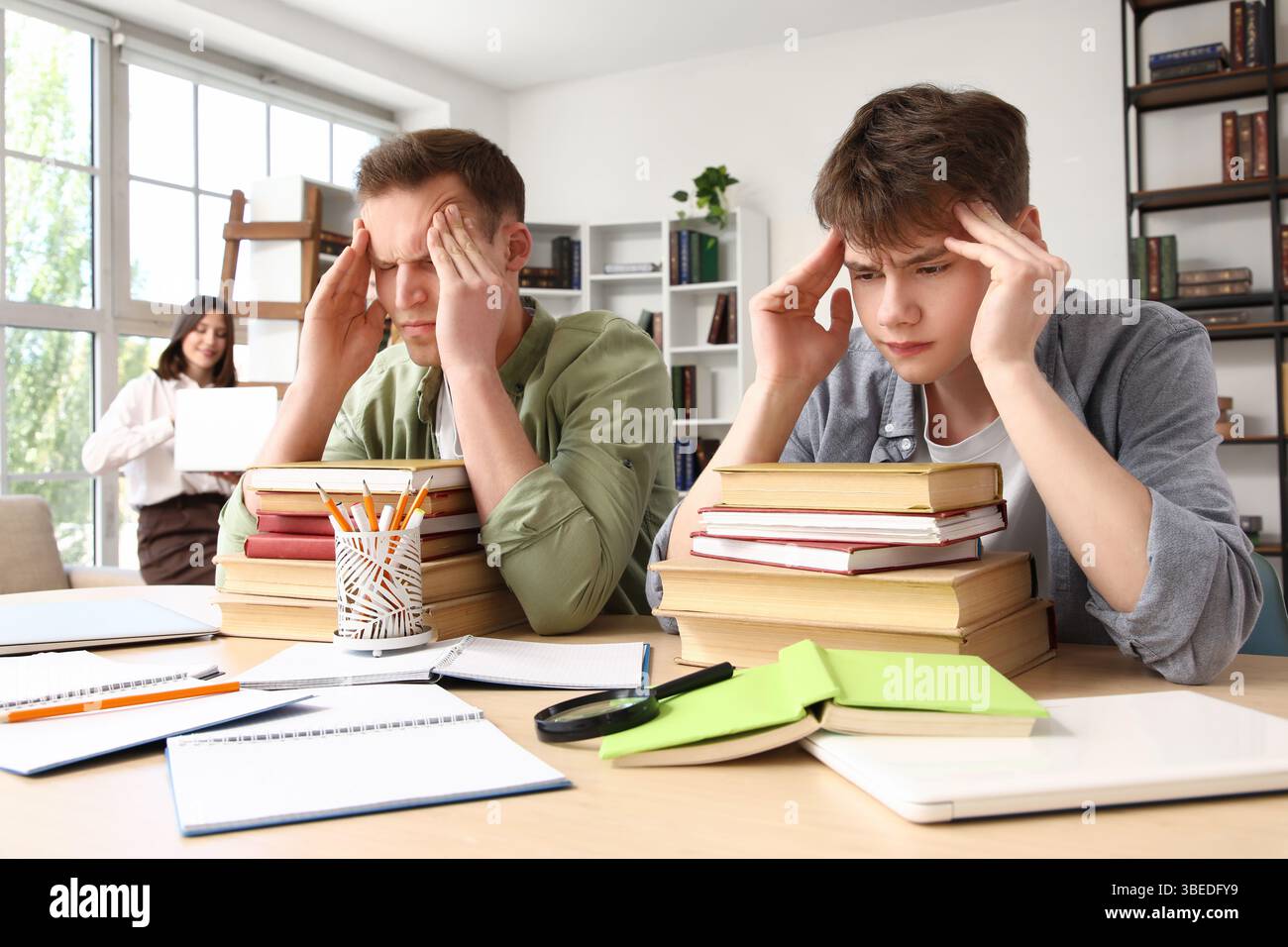 Stressed male students with books at table in library Stock Photo - Alamy