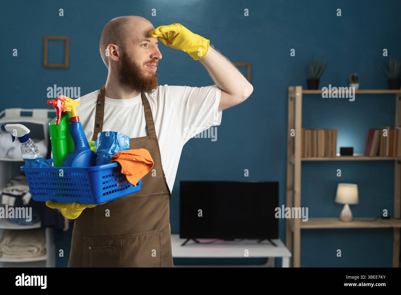 Janitor bearded man holding basket with cleaning supplies looking away ...