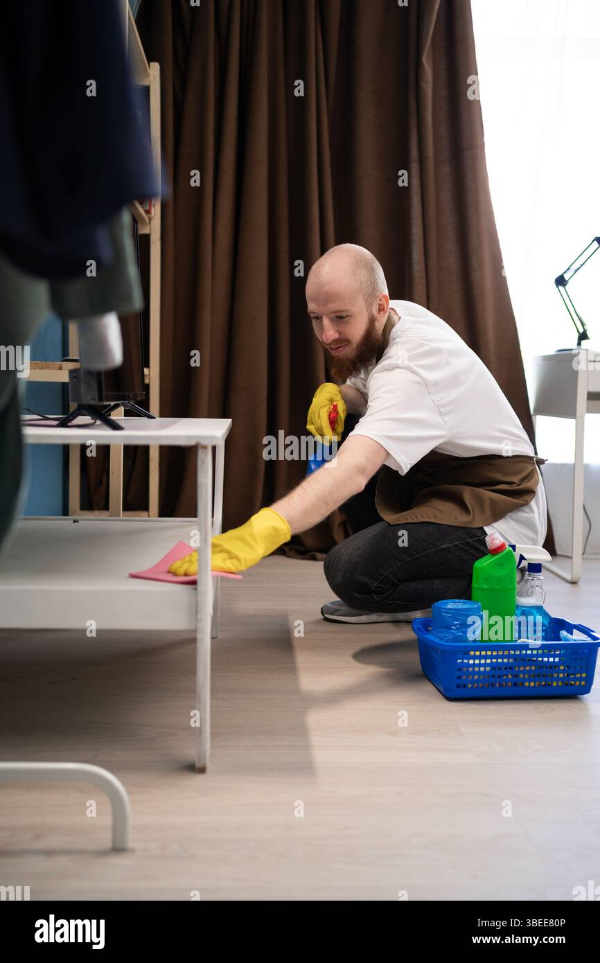 Bearded man in rubber gloves wiping dust from TV stand showing concept ...