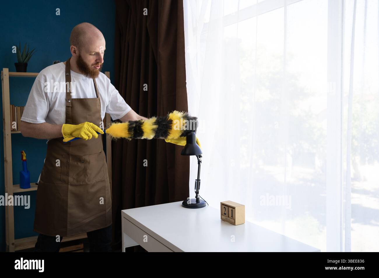 Man using feather duster to wipe dust from lamp in living room showing ...