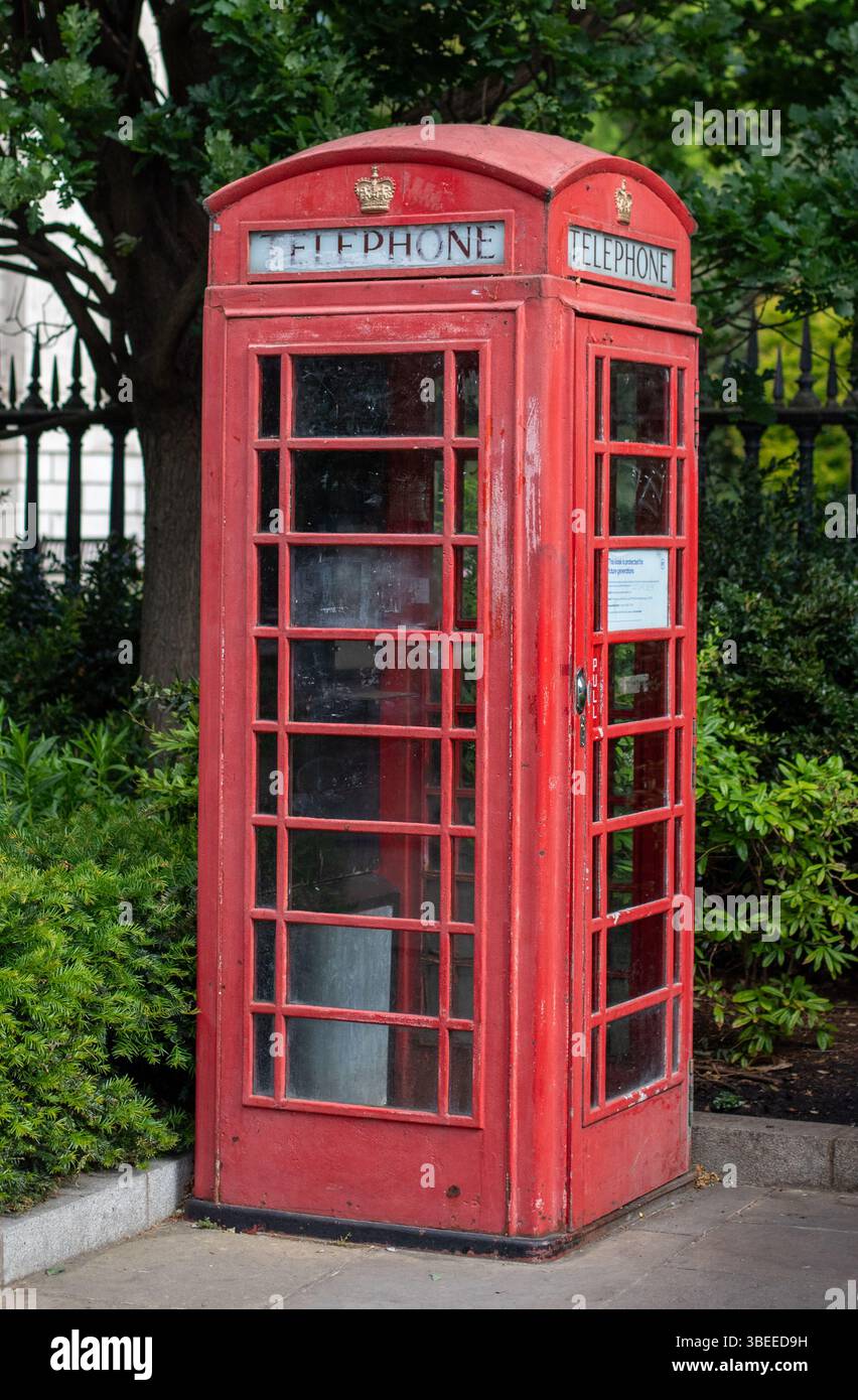 A classic red British telephone booth surrounded by greenery in a ...