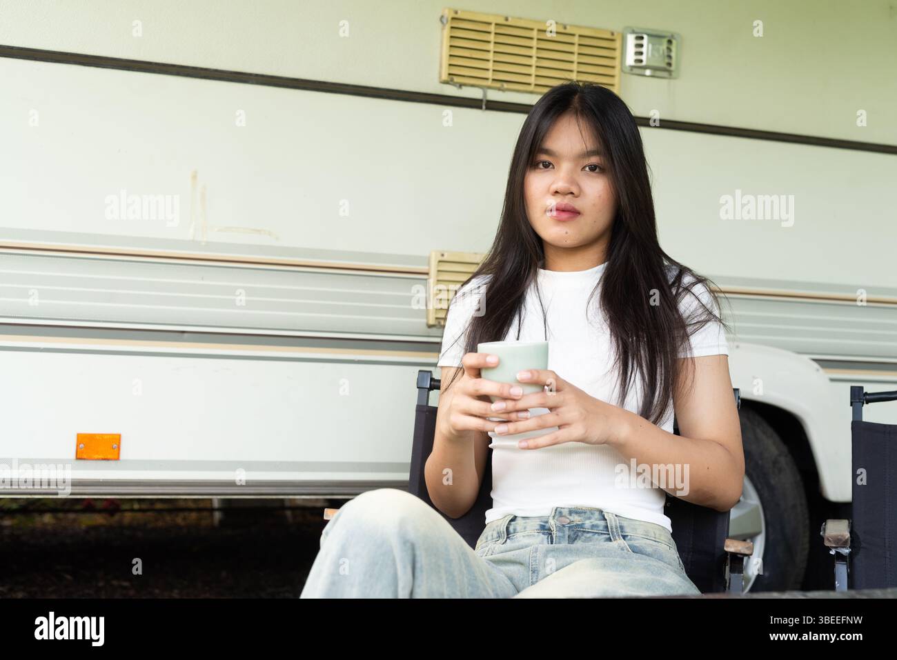 Young woman sitting outside of motorhome RV vehicle in camping site ...
