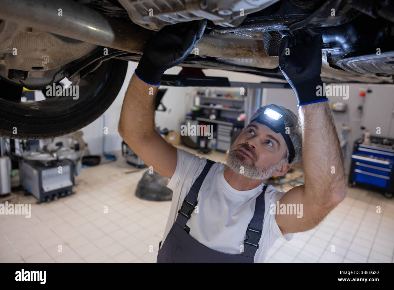 Mechanic inspecting undercarriage with headlamp Stock Photo - Alamy
