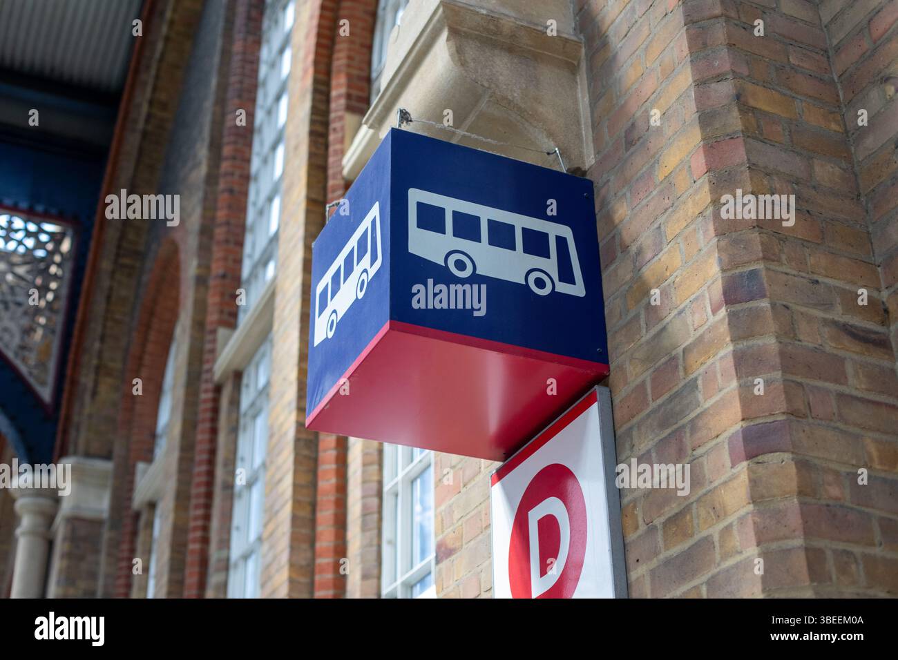 A bus stop sign hangs at a train station in London, UK. The brick wall ...
