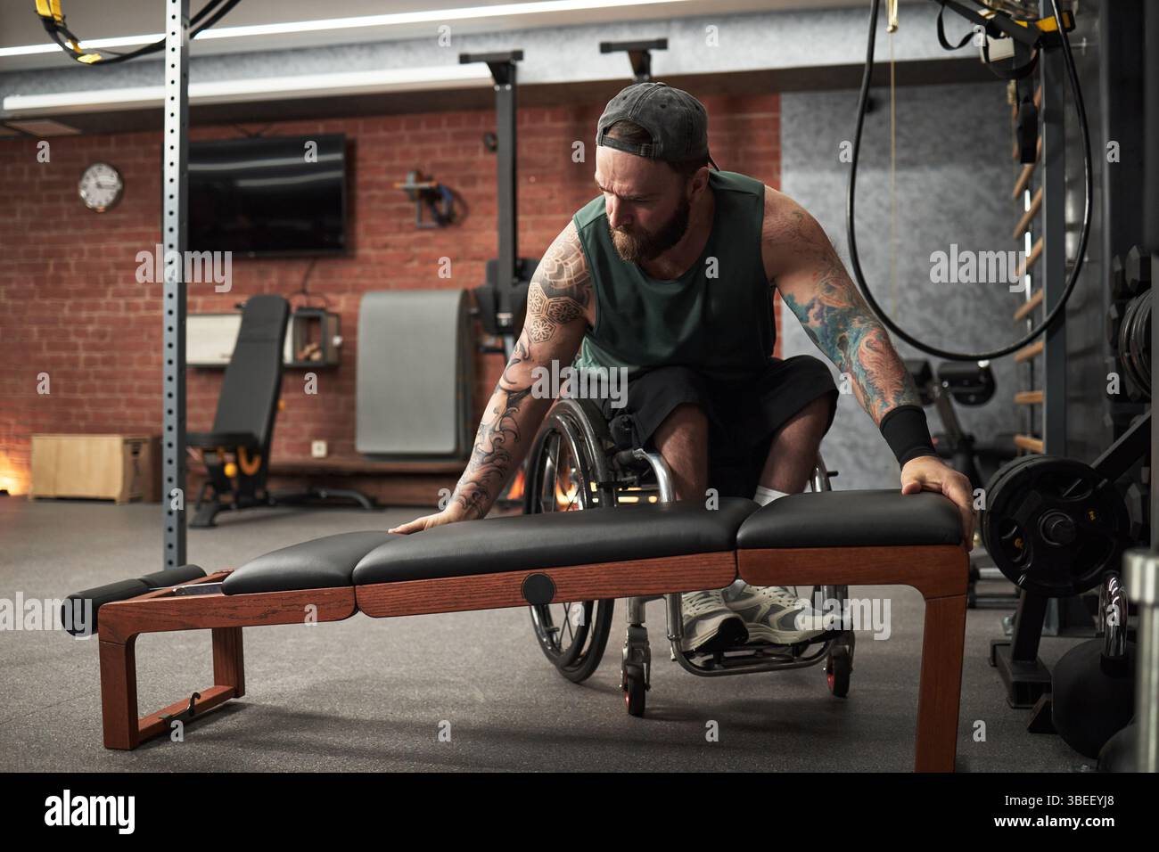 Man with tattoos in wheelchair adjusting gym bench before starting ...