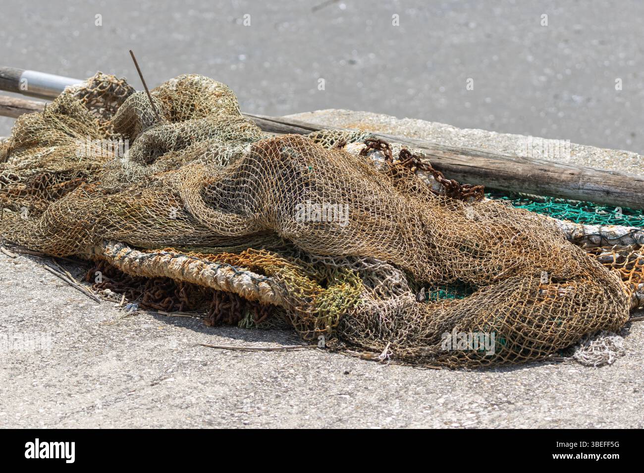 Pile of fishing nets drying on a concrete dock near a rusty chain and ...