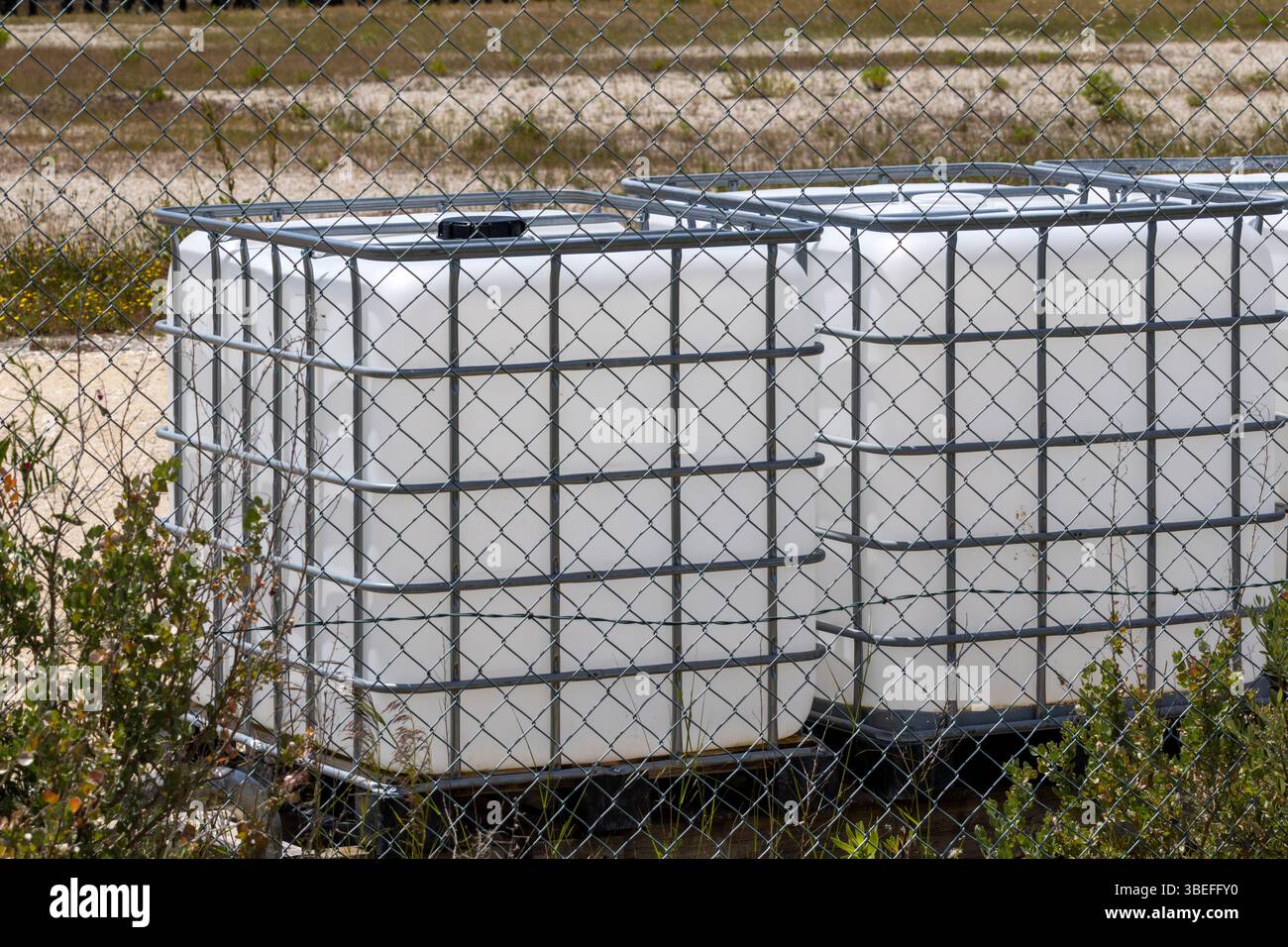 Two white ibc totes behind a chain link fence storing water or ...