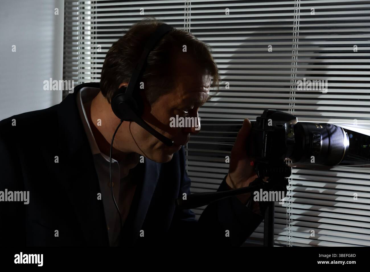 The man conducts covert surveillance through the blinds using a camera ...