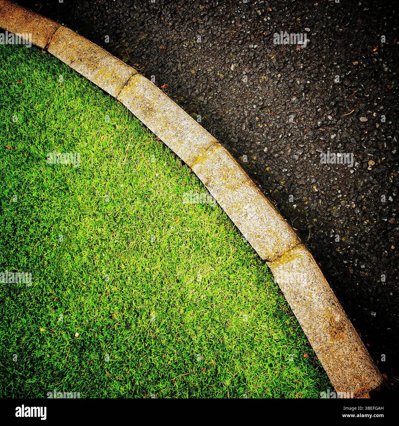 The vibrant green grass curves smoothly alongside a dark asphalt pathway, creating a pleasing ...