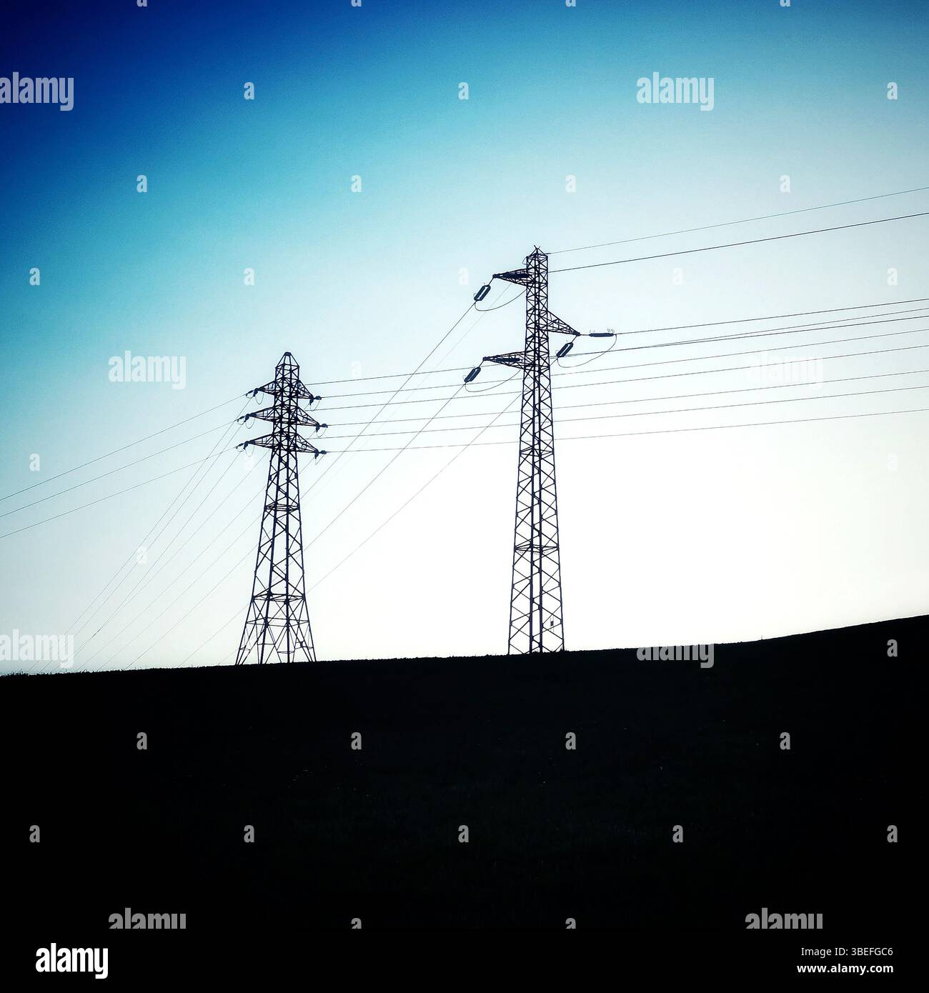 Two power towers reach upwards, silhouetted against a transitioning ...