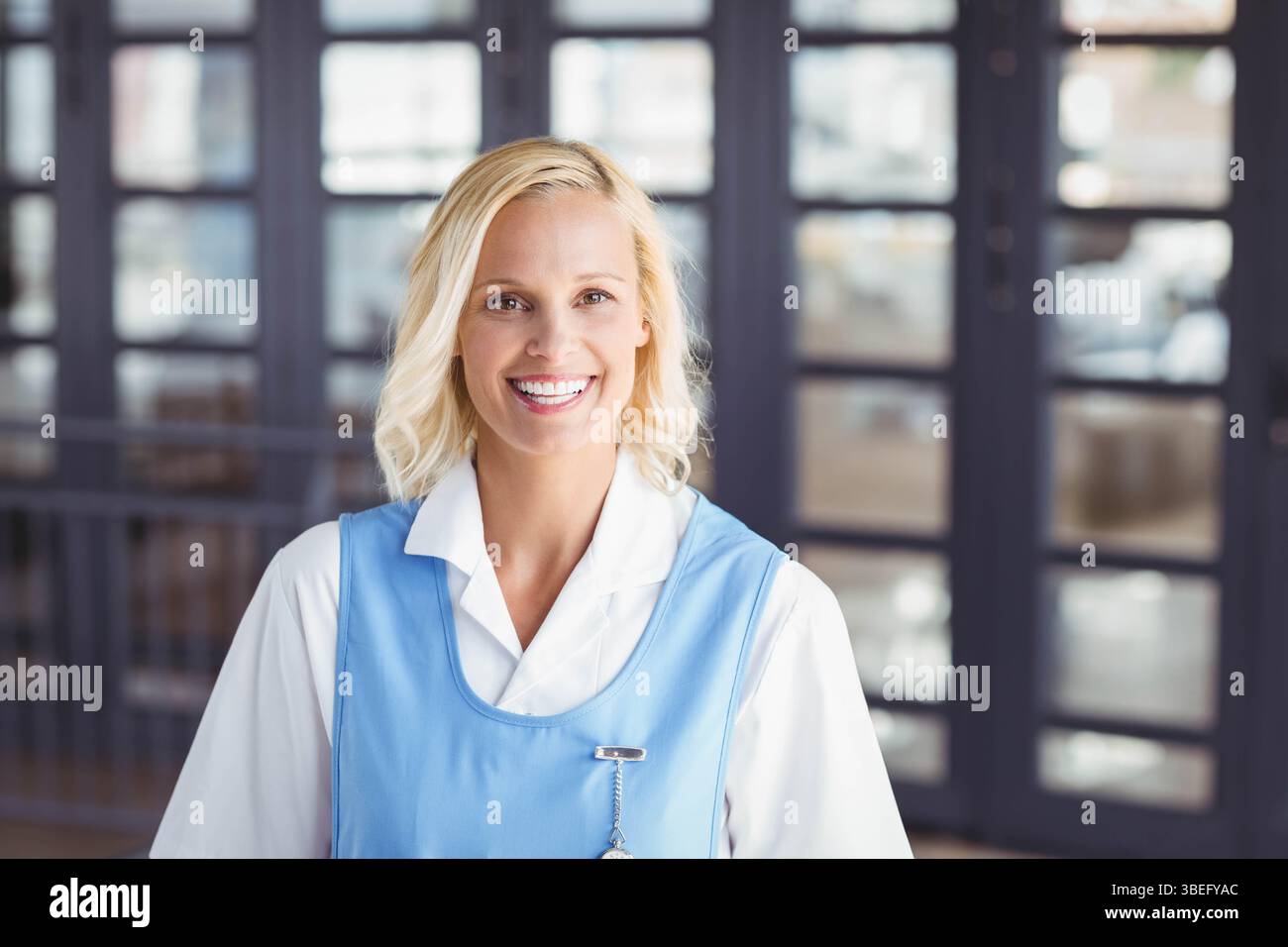 Middle-aged female hotel staff member standing in blue smock at lobby ...