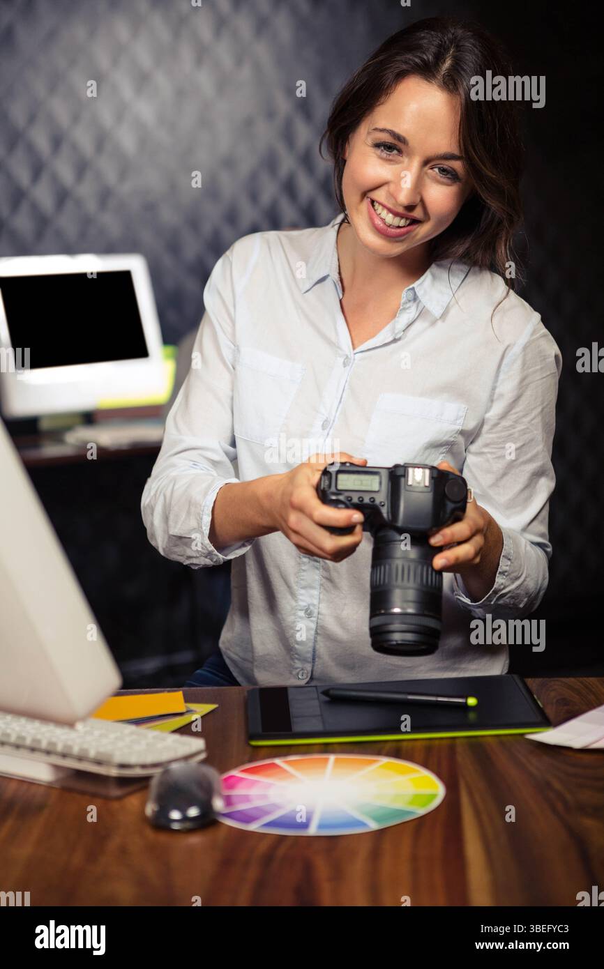 Woman standing behind desk in studio workspace, holding DSLR camera ...