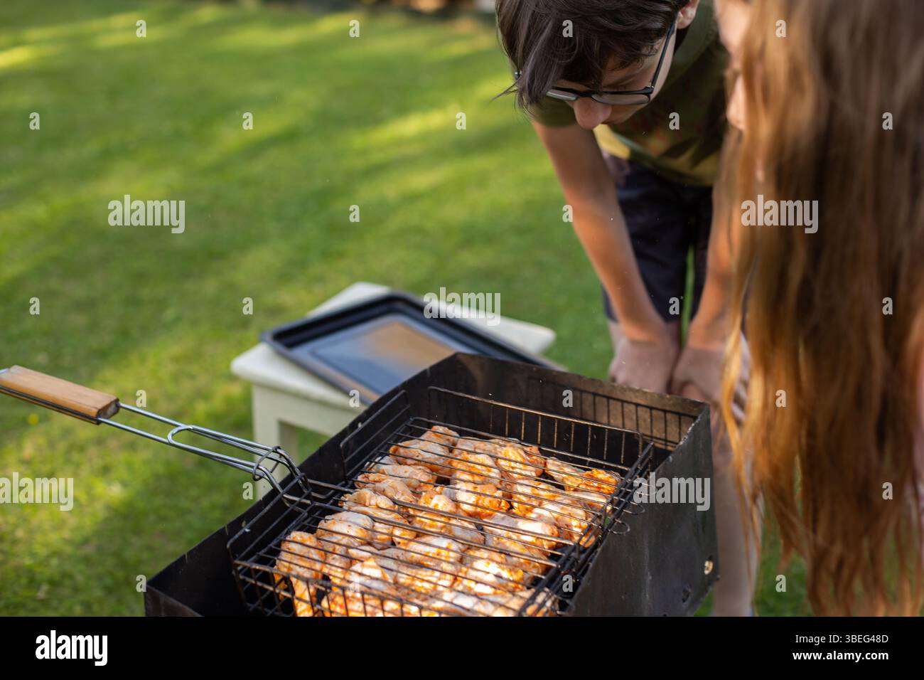 Happy kids grilling chicken on a barbecue grill in a backyard during ...