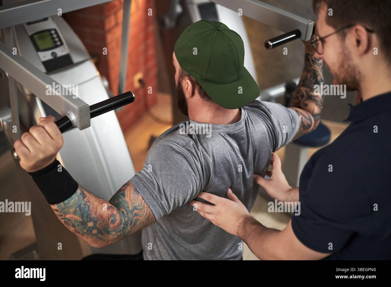 Athlete lifting weights on gym machine under supervision of personal ...