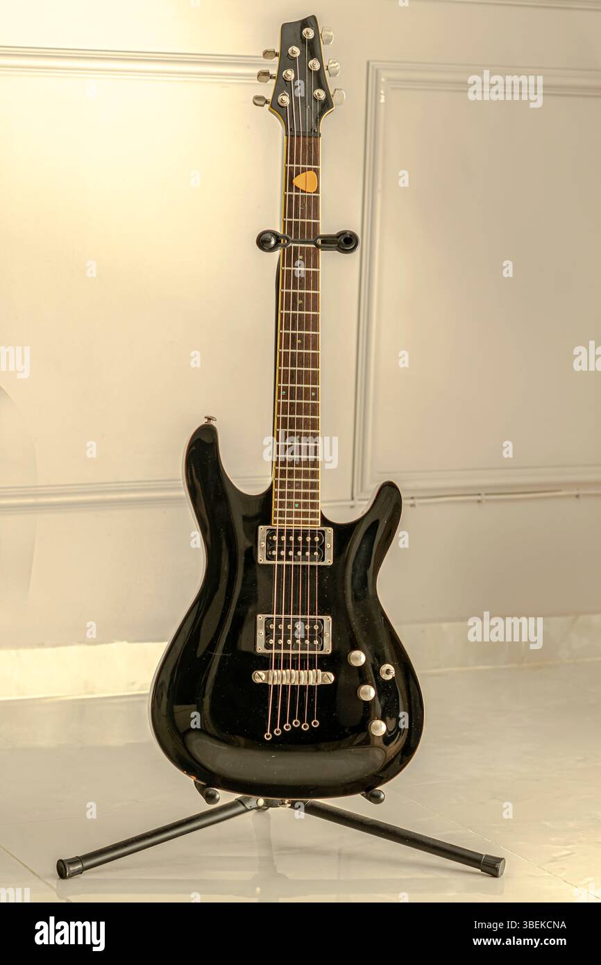 A black electric guitar with chrome tone control knobs on a stand ...