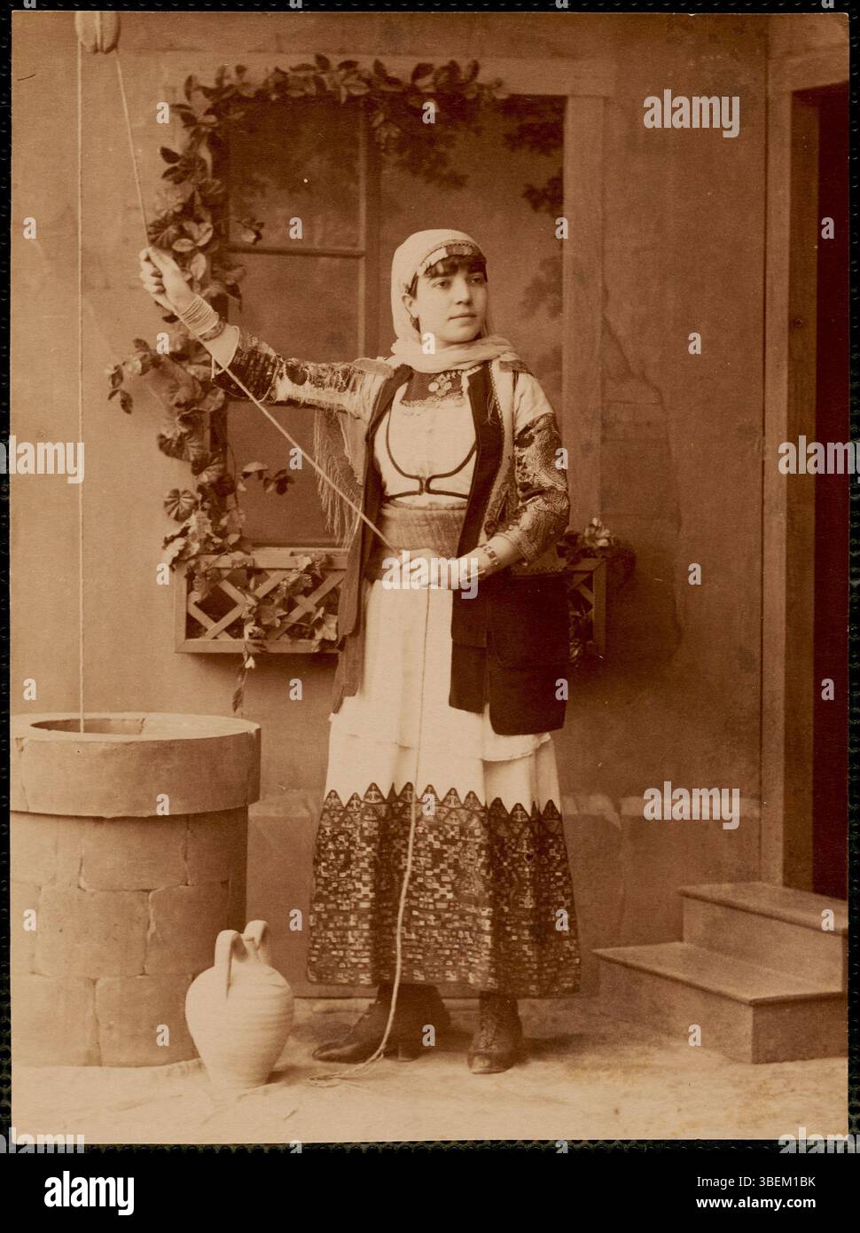 Studio portrait of a woman in traditional Greek dress posed beside a ...
