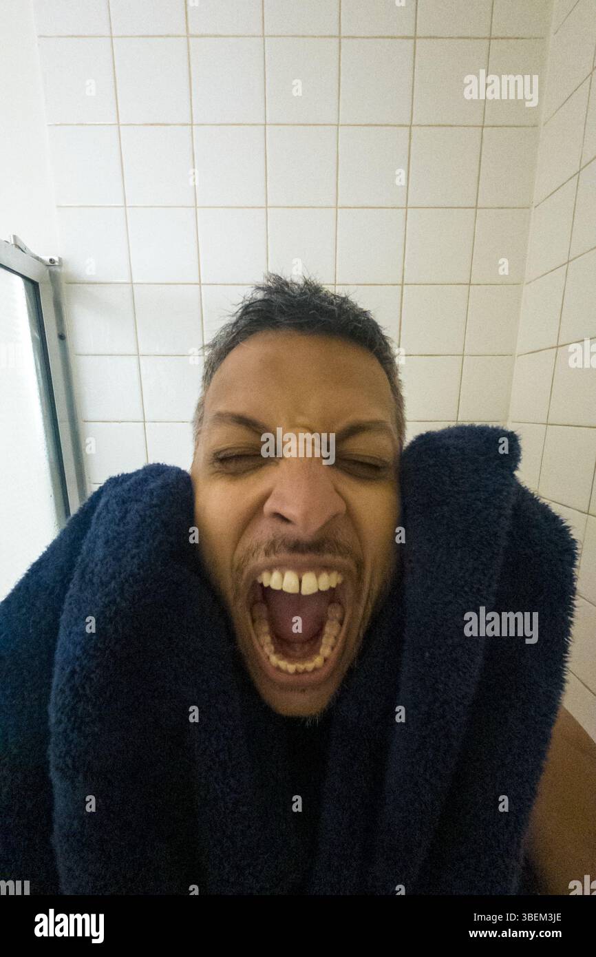 A man is in a bathroom with a towel wrapped around his face. He is making a funny face and ...