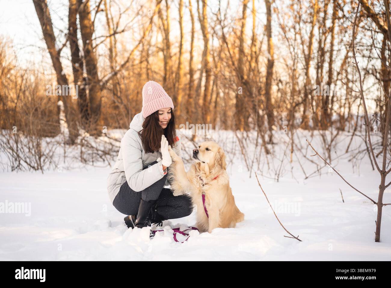 A woman in a winter outfit joyfully interacts with her golden retriever ...