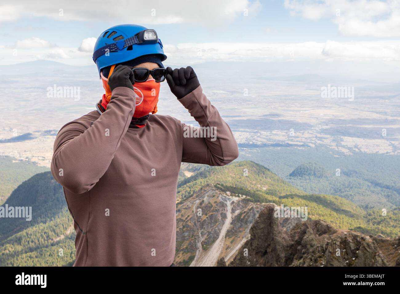 A hiker wearing a helmet, sunglasses, and protective gear adjusts his ...