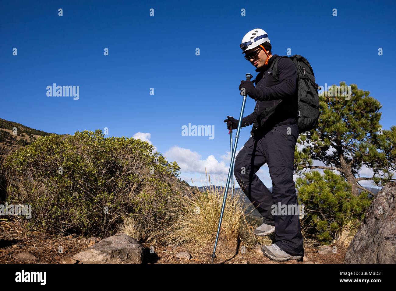 A hiker wearing outdoor gear and a helmet walks with trekking poles on ...