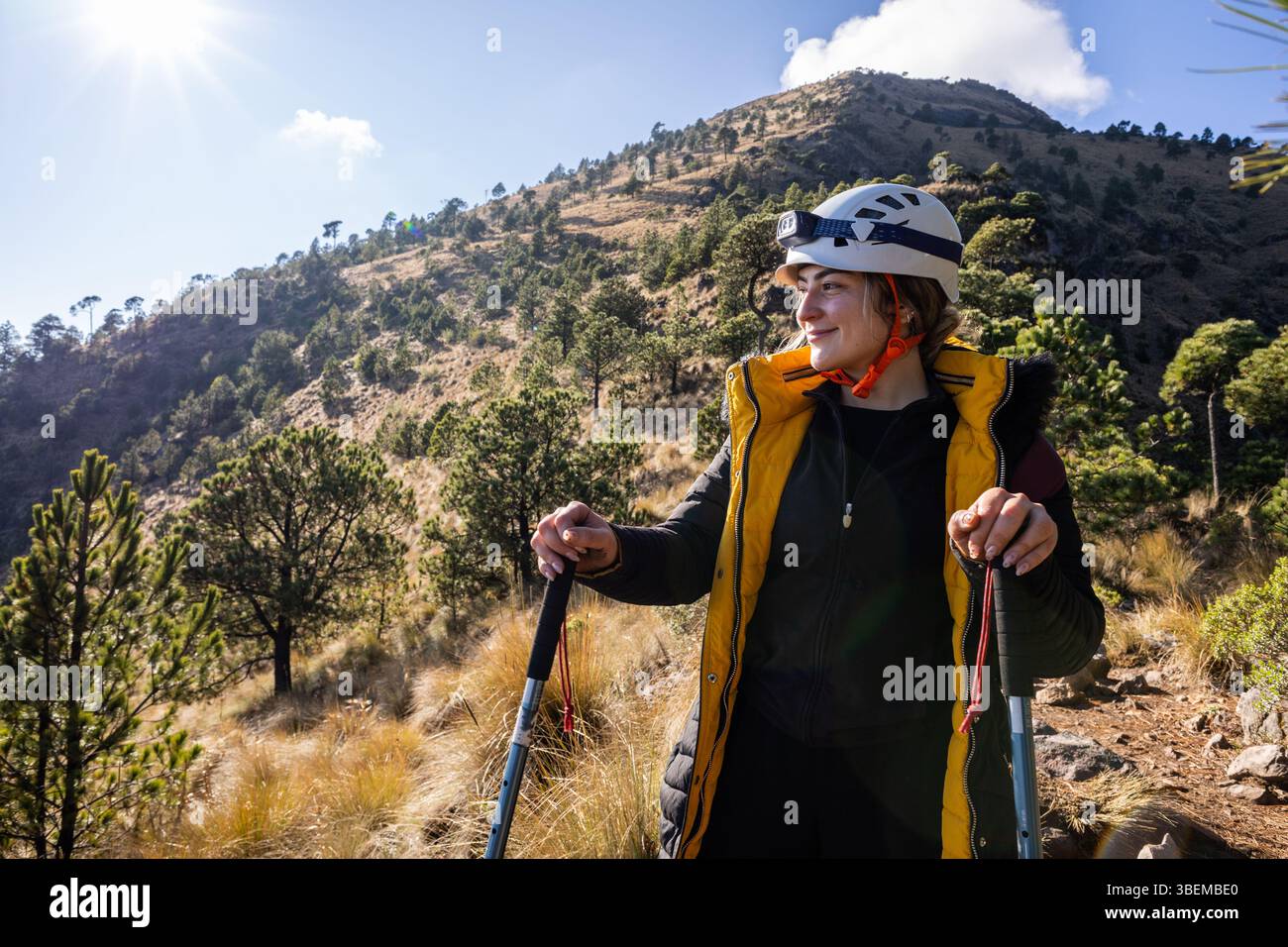 Female hiker whit helmet, holding trekking poles, smiles while enjoying ...