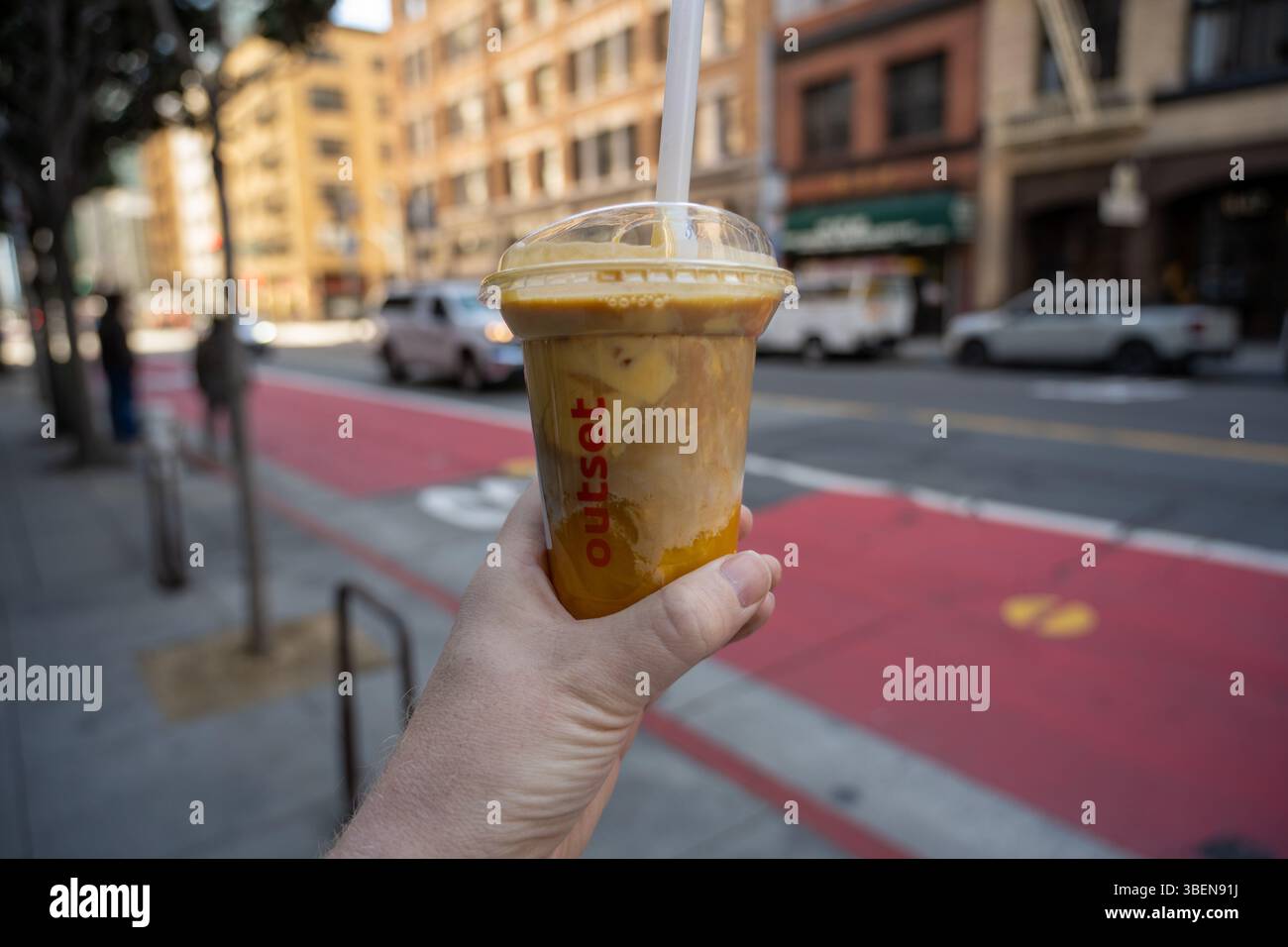 Close-up of a person's hand holding an iced Outset Coffee mango latte ...