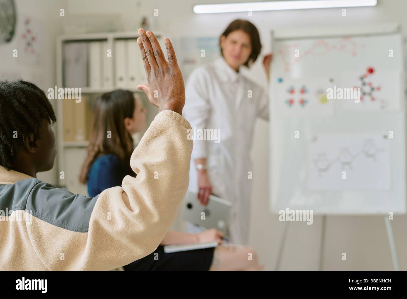 Student raising hand during classroom session led by female teacher who ...