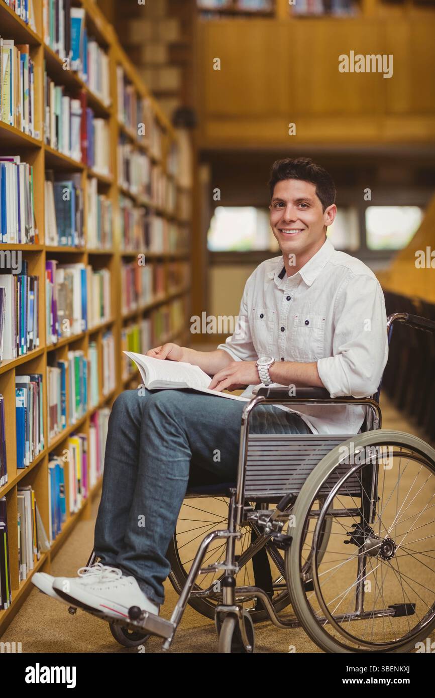 Teenage man sitting in wheelchair reading open book amid wooden ...