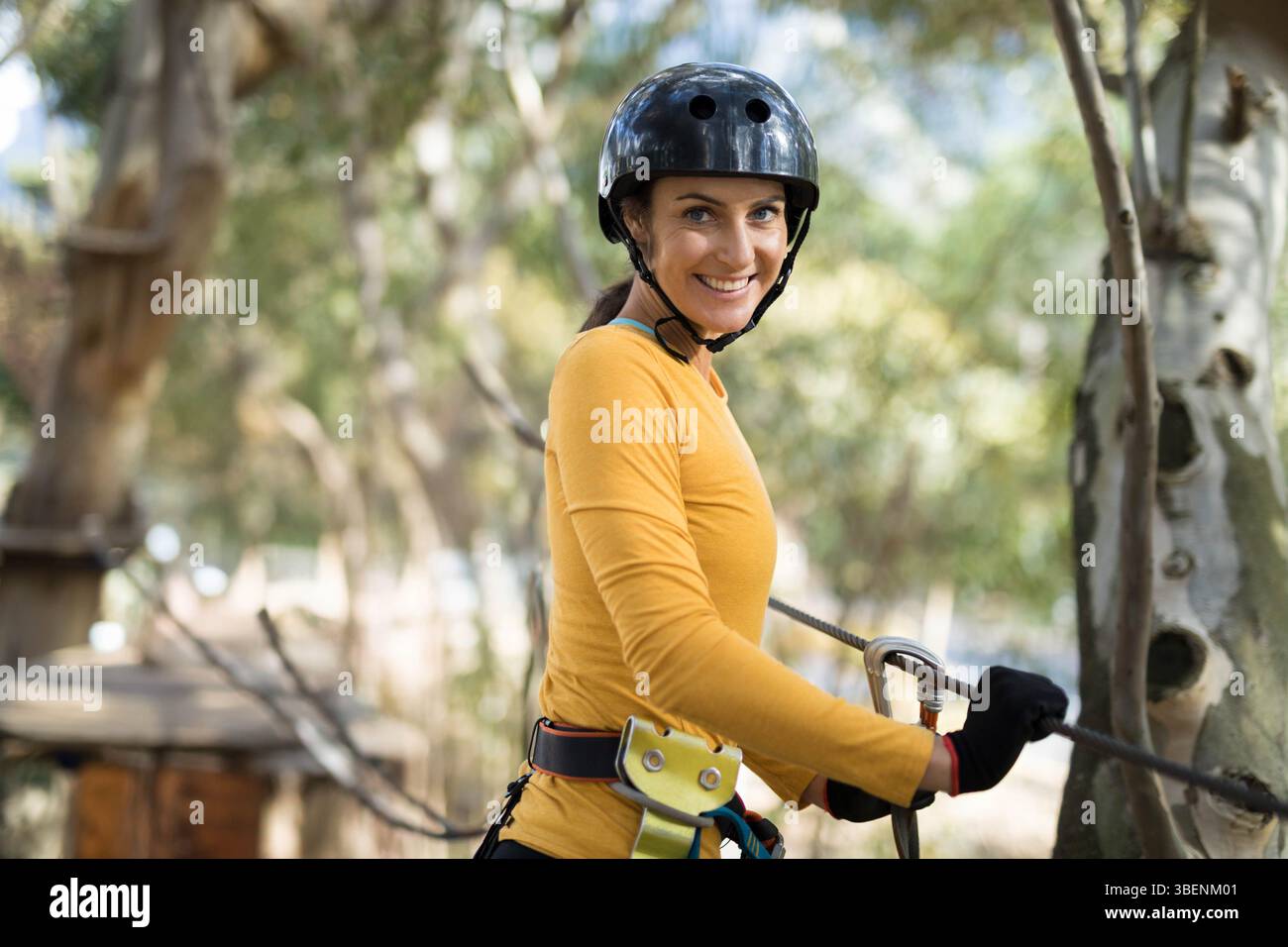 Woman navigating treetop rope course in wooded adventure park wearing ...