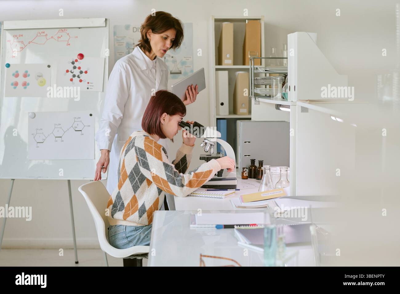 Teacher guiding student as she using microscope in classroom during ...