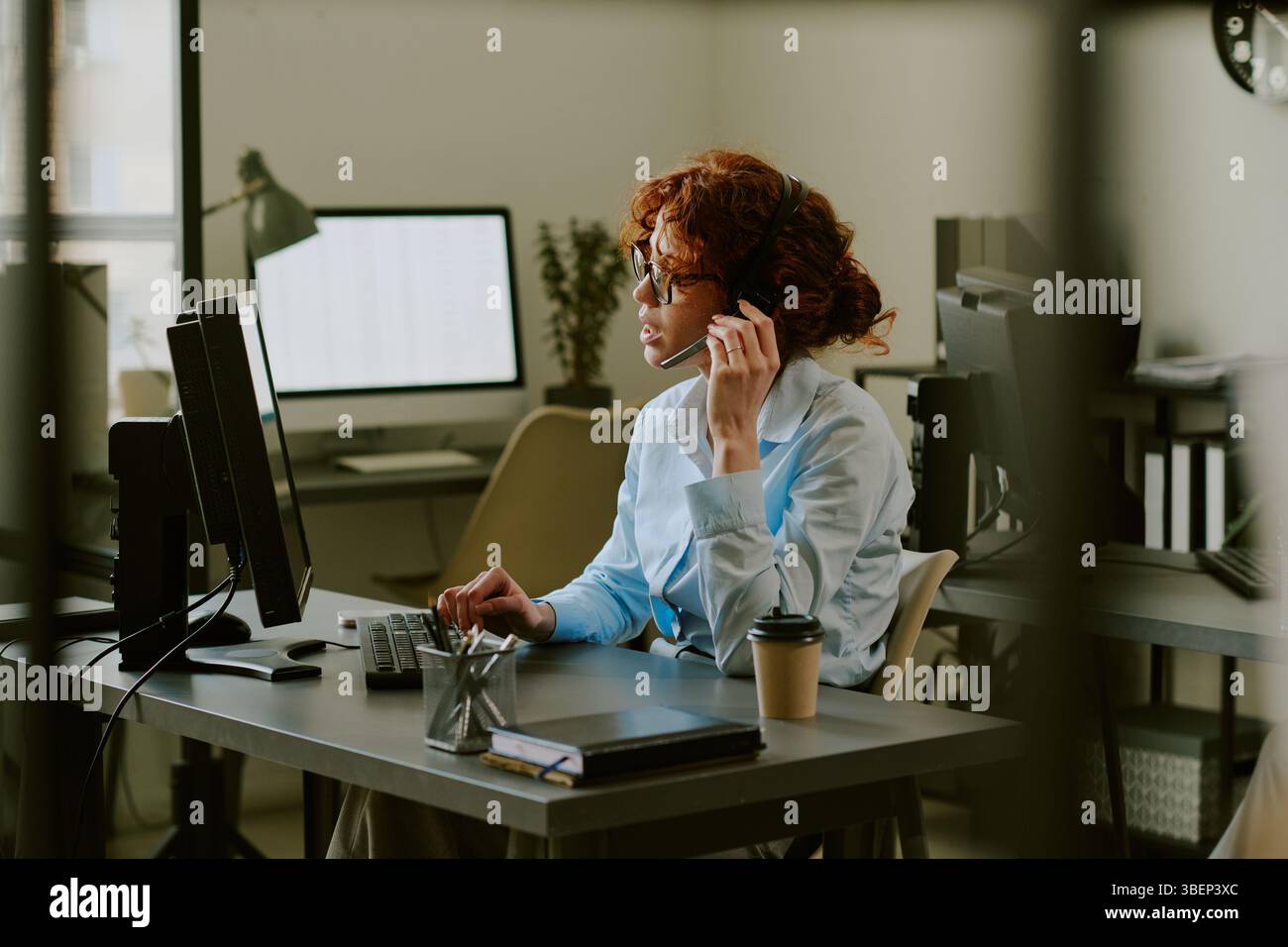 Businesswoman speaking on headset while working in office at desk with ...