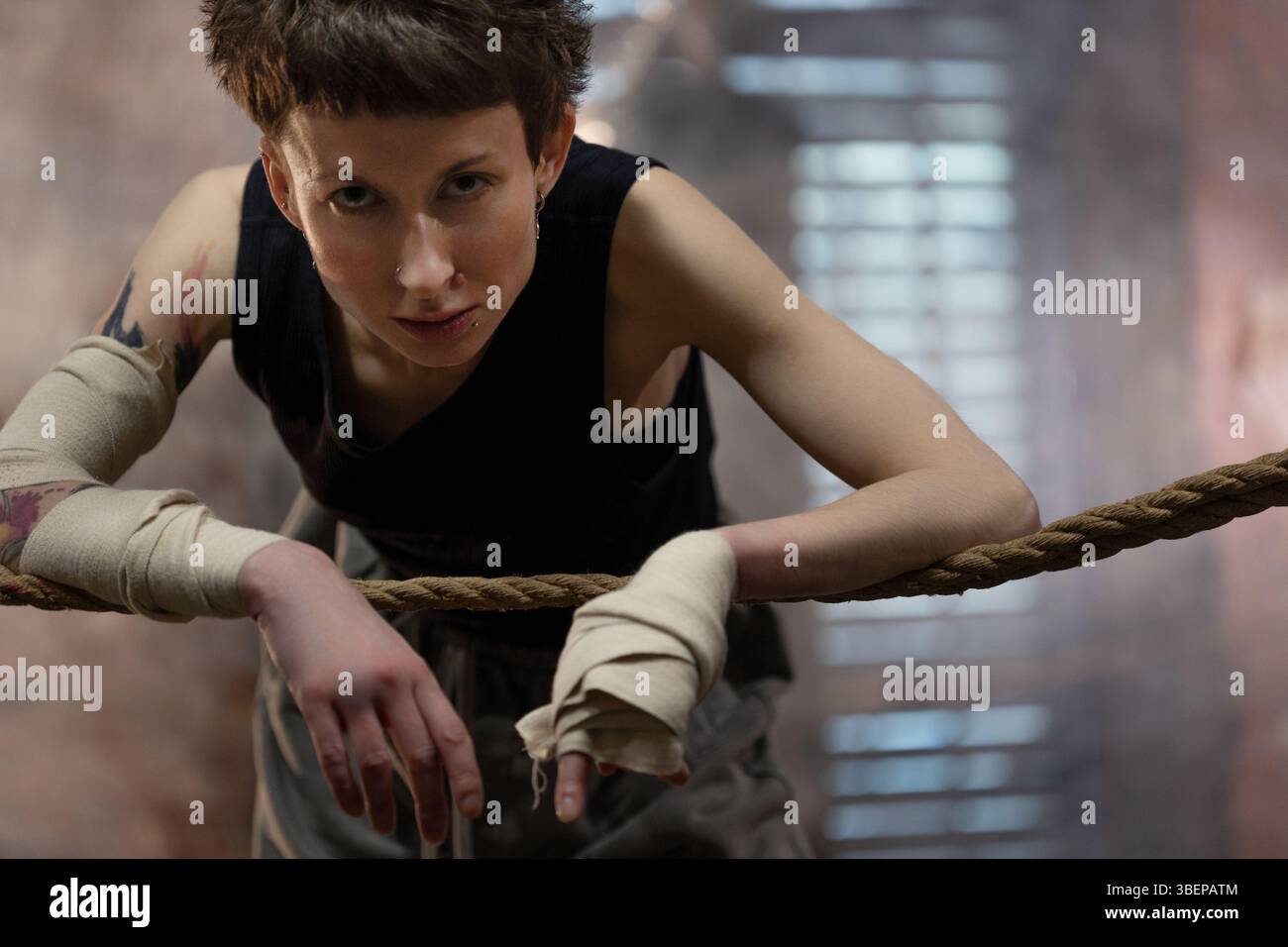 Female boxer with short hair pausing workout, leaning on ring ropes ...