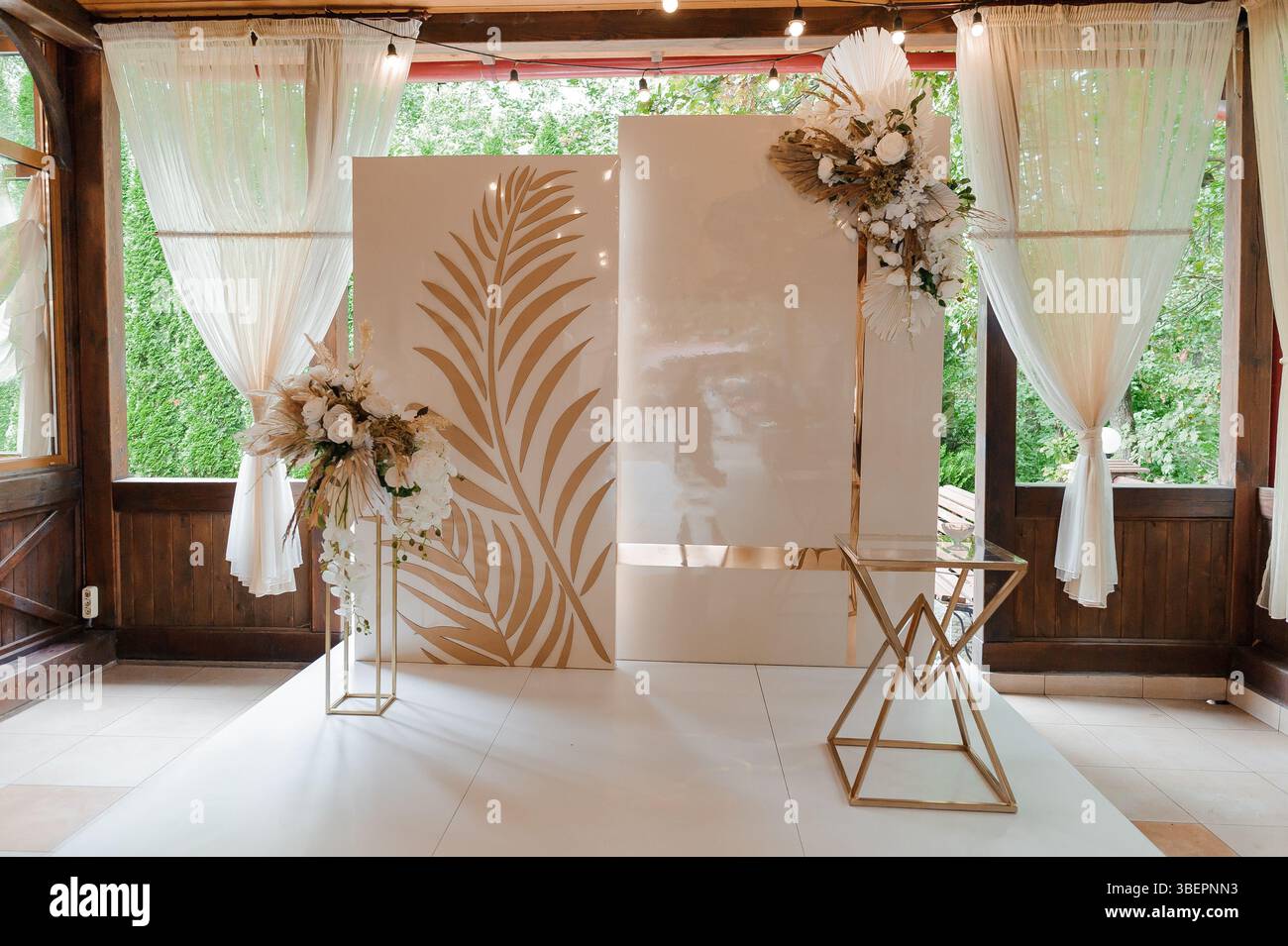 Elegant wedding ceremony setup with a white backdrop featuring golden ...